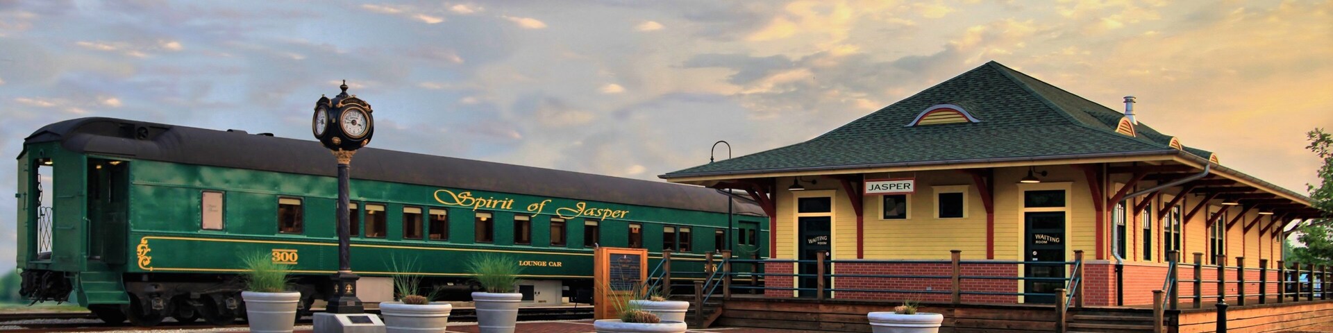 Uma estação de trem antiga com um trem verde identificado como 'Spirit of Jasper' e uma sala de espera.