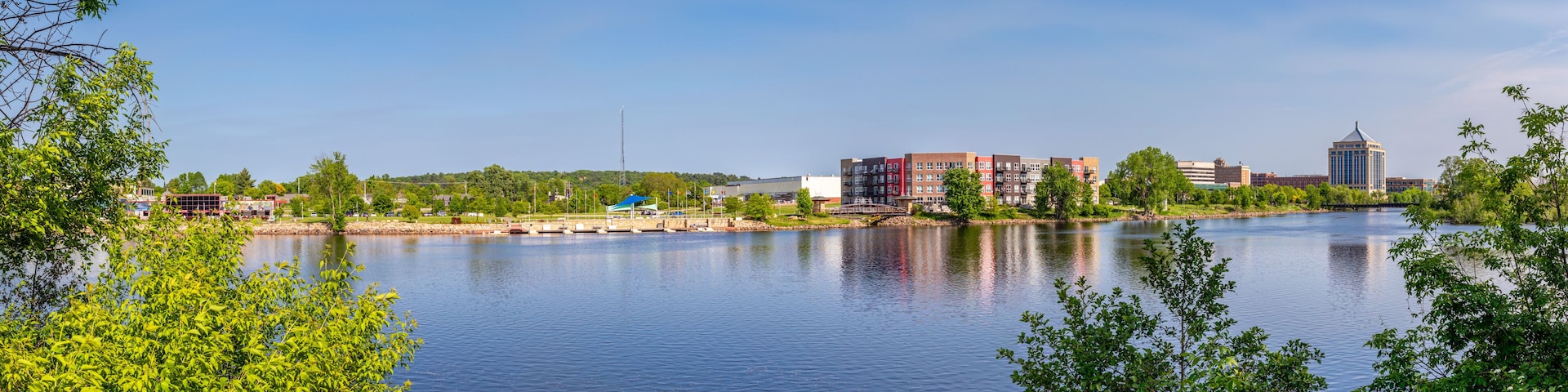 Um lago calmo com edifícios e árvores ao fundo.