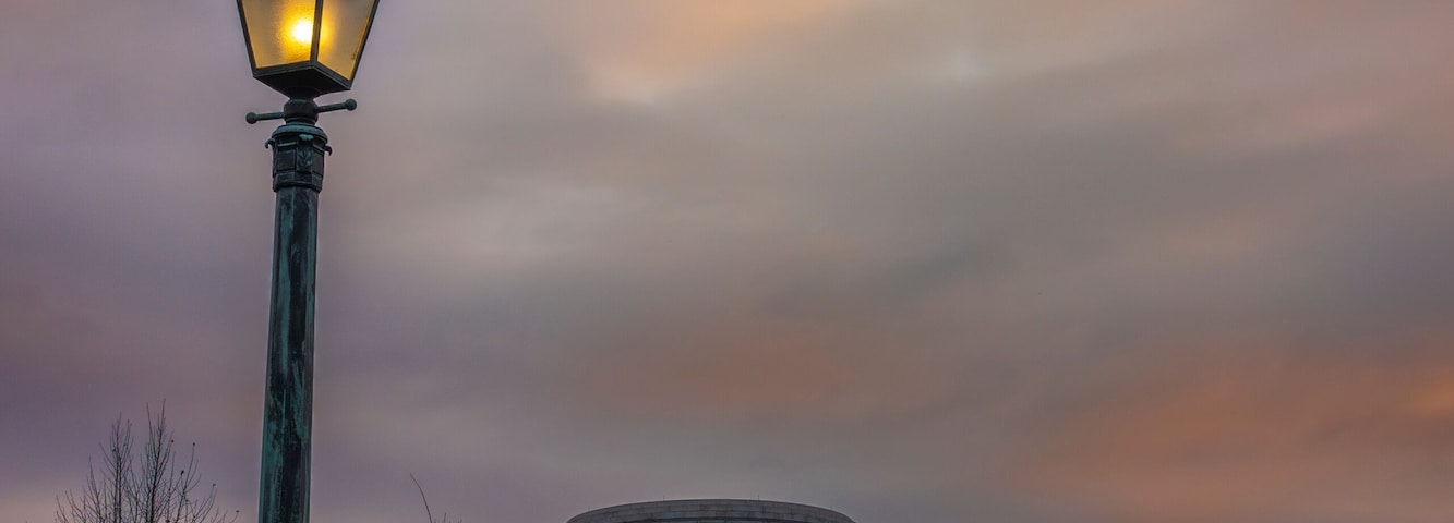 Um edifício histórico com colunas, um poste de luz e um campo gramado.