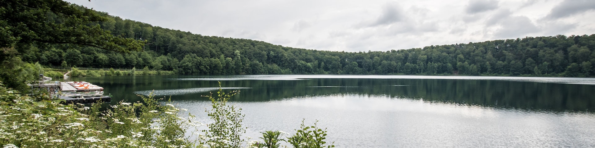 Um lago calmo rodeado por uma floresta densa, com um barco atracado à esquerda.