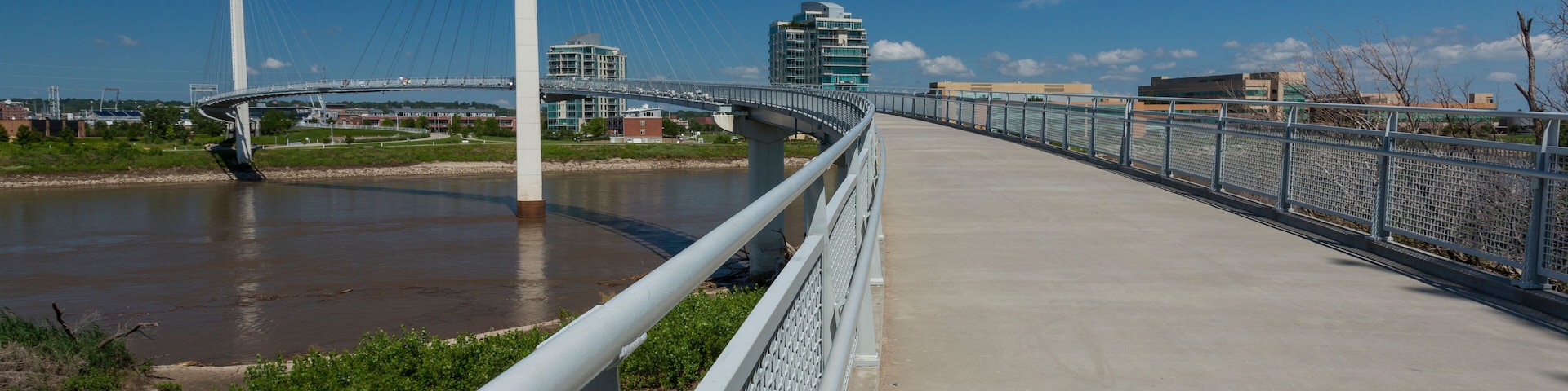 Uma ponte para pedestres sobre um rio, com uma ponte moderna suspensa ao fundo.