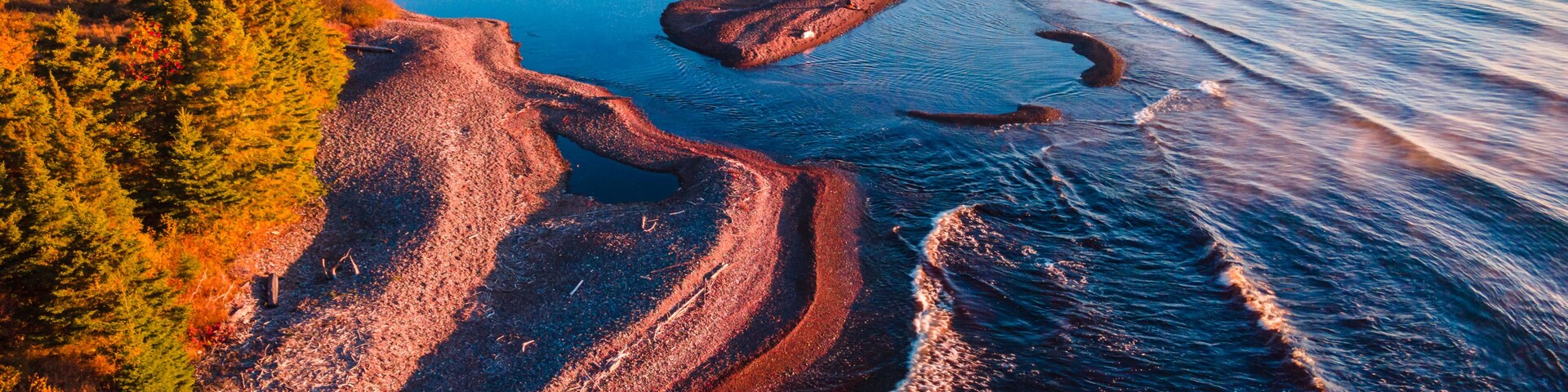Paisagem costeira com um rio que deságua no mar, rodeada por florestas densas com folhagem outonal.
