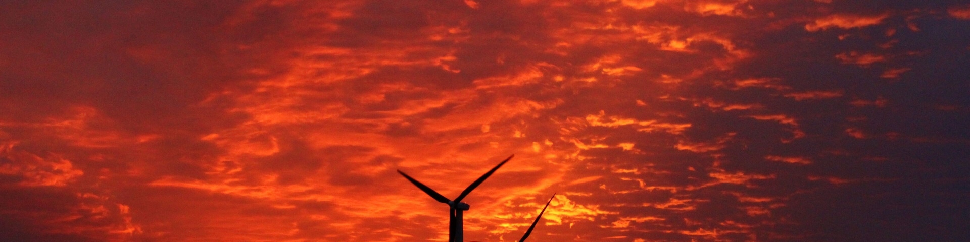 Silhuetas de turbinas eólicas contra um céu vibrante ao pôr do sol.