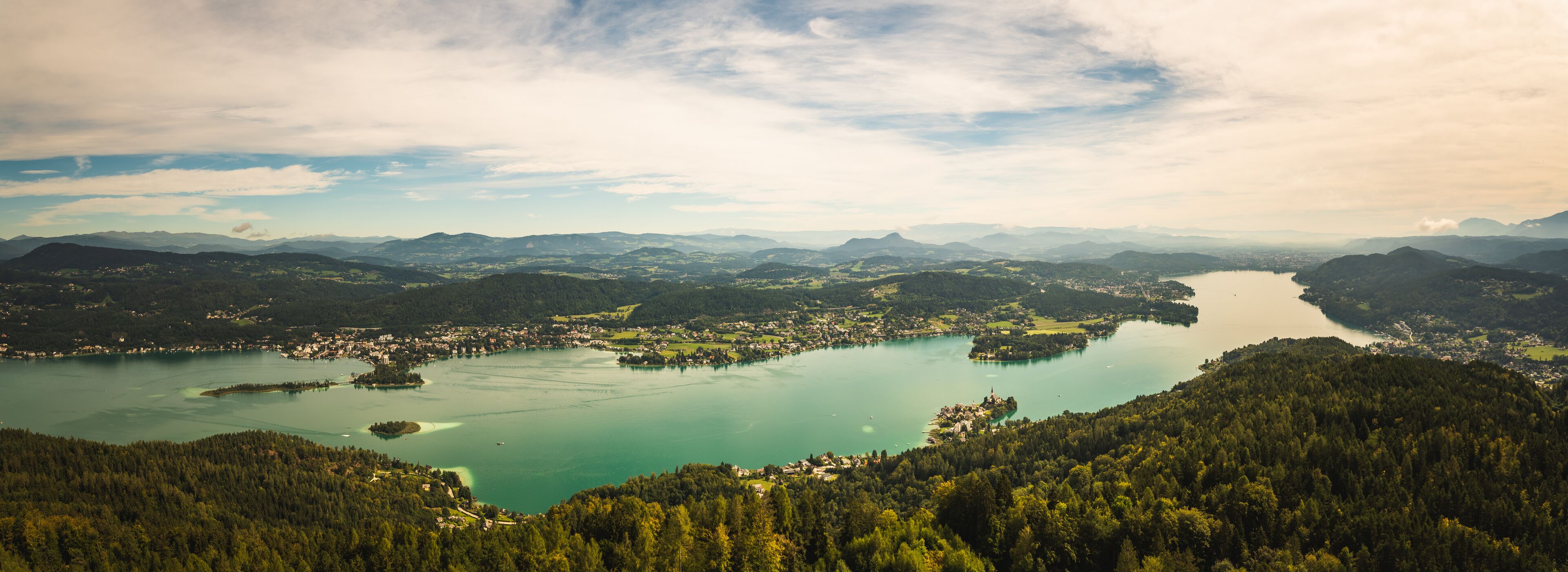 Vista panorâmica de um lago rodeado por colinas arborizadas e uma pequena cidade.