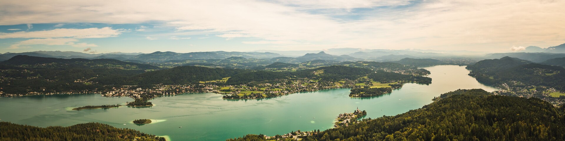 Vista panorâmica de um lago rodeado por colinas arborizadas e uma pequena cidade.