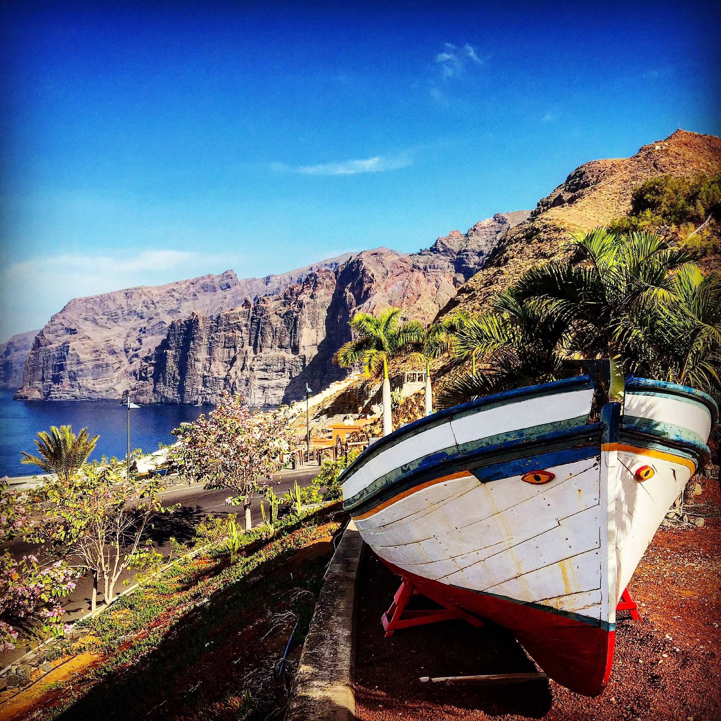 Paisagem costeira com um penhasco rochoso, um pequeno barco e céu azul límpido.