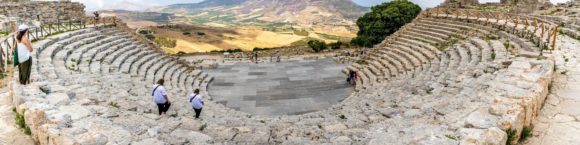Um antigo anfiteatro com assentos de pedra e montanhas ao fundo.