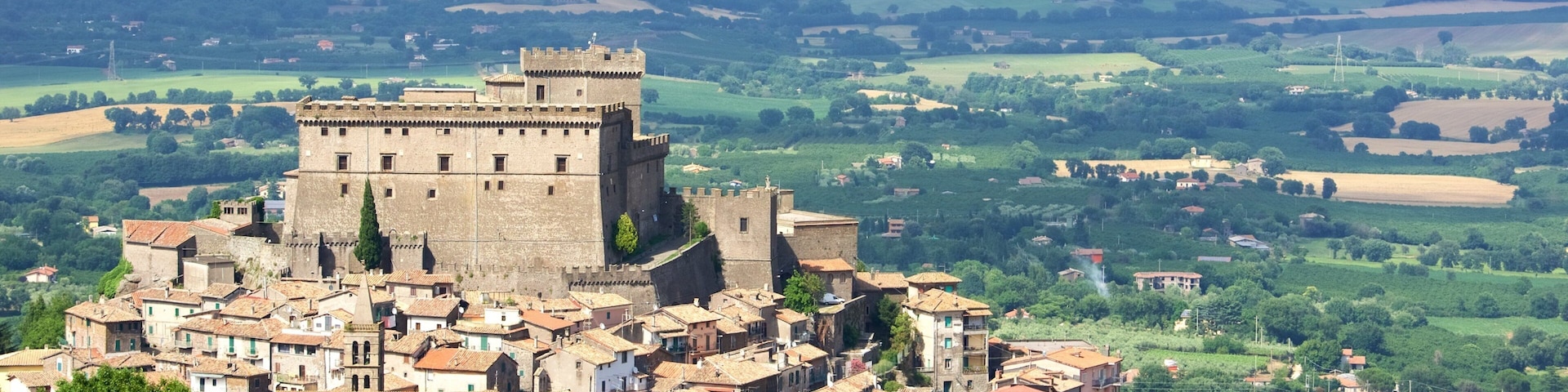 Um castelo medieval no topo de uma colina, com vista para uma cidade histórica com edifícios de telhado em terracota.
