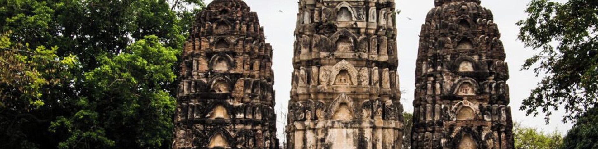 Um templo com três torres, rodeado por árvores e um muro de tijolos.