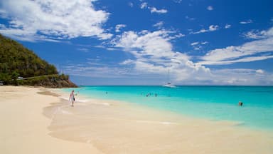 Uma praia com águas turquesa cristalinas, areal arenoso e um veleiro ao longe.