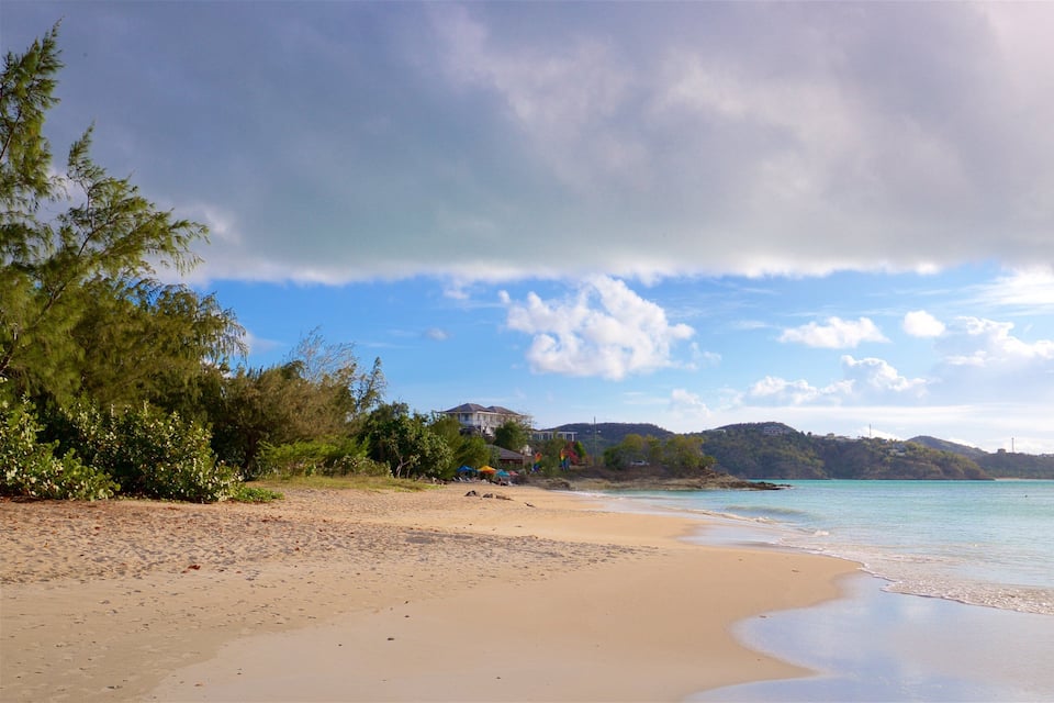 Praia arenosa com águas turquesa cristalinas, rodeada por vegetação exuberante e colinas ao fundo.