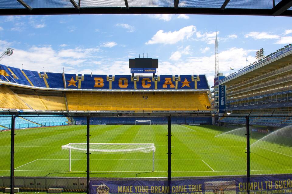 Um estádio de futebol com assentos em azul e amarelo, um campo verde e um gol.
