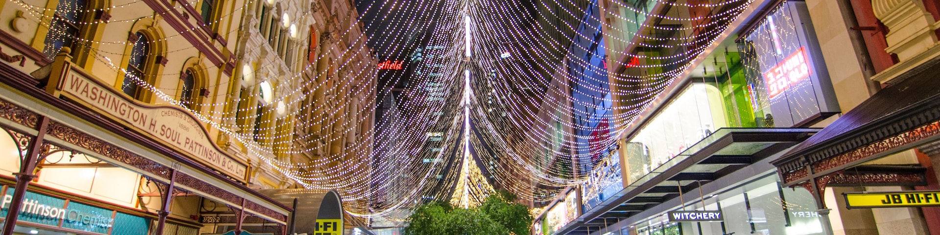 Rua molhada com luzes de Natal e lojas.