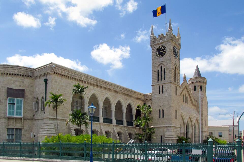 Um edifício histórico com uma torre do relógio, janelas em arco e uma bandeira.