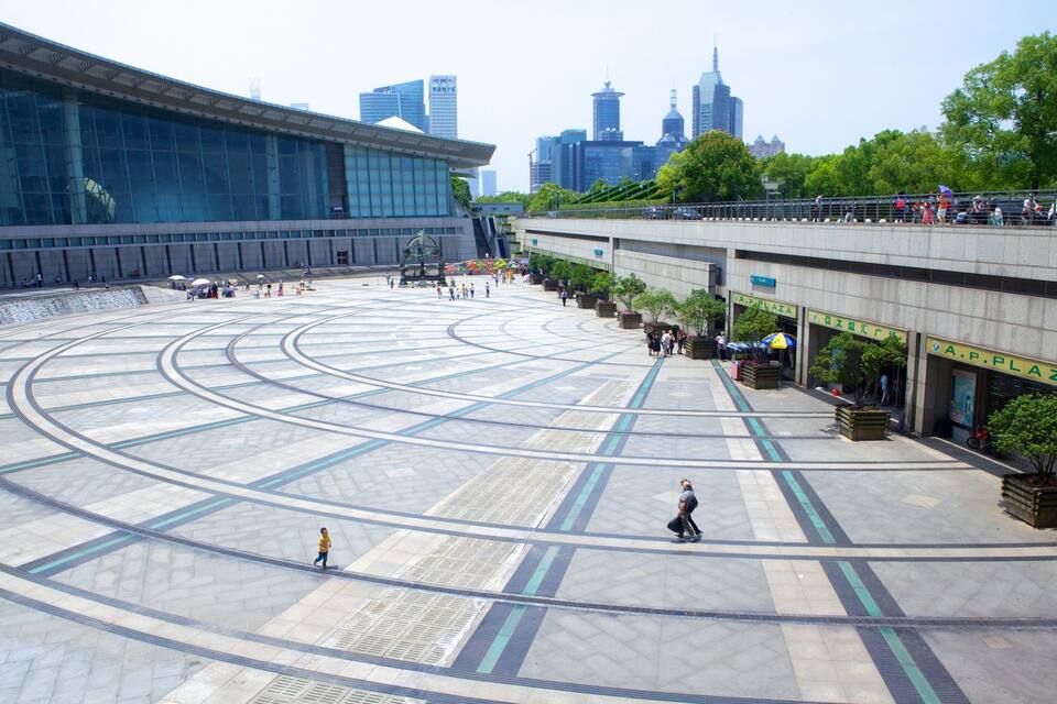 Uma grande praça aberta com um edifício moderno e um horizonte urbano ao fundo.