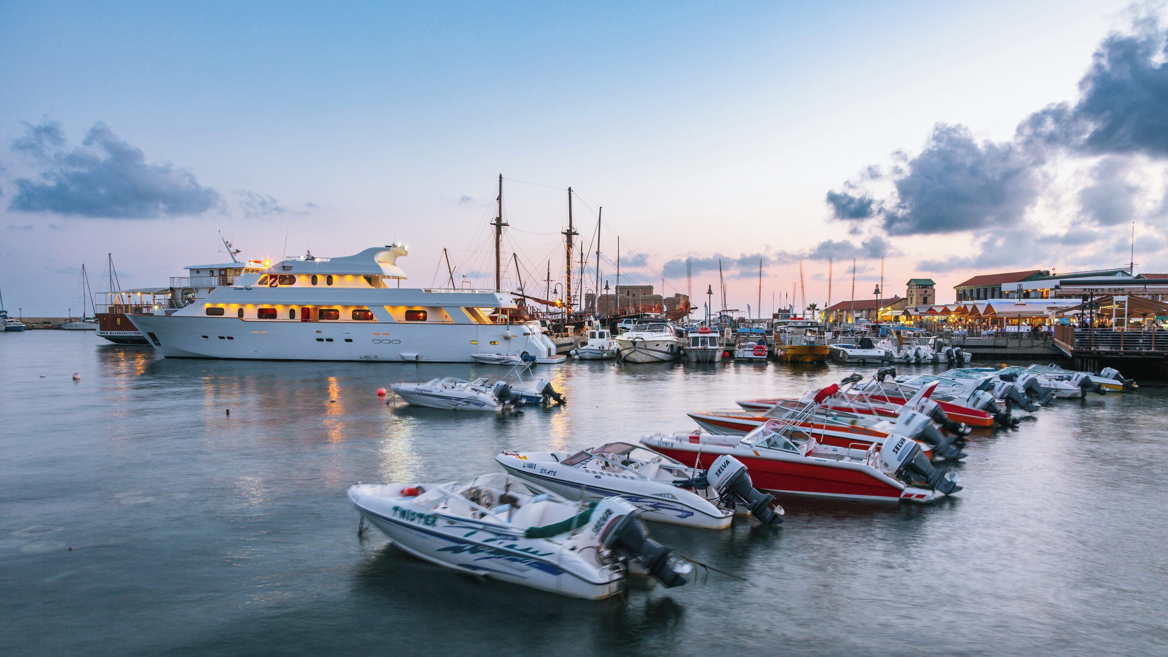Visiting Paphos Harbour in Cyprus during sunset with yachts and fishing boats docked at the tranquil water's edge
