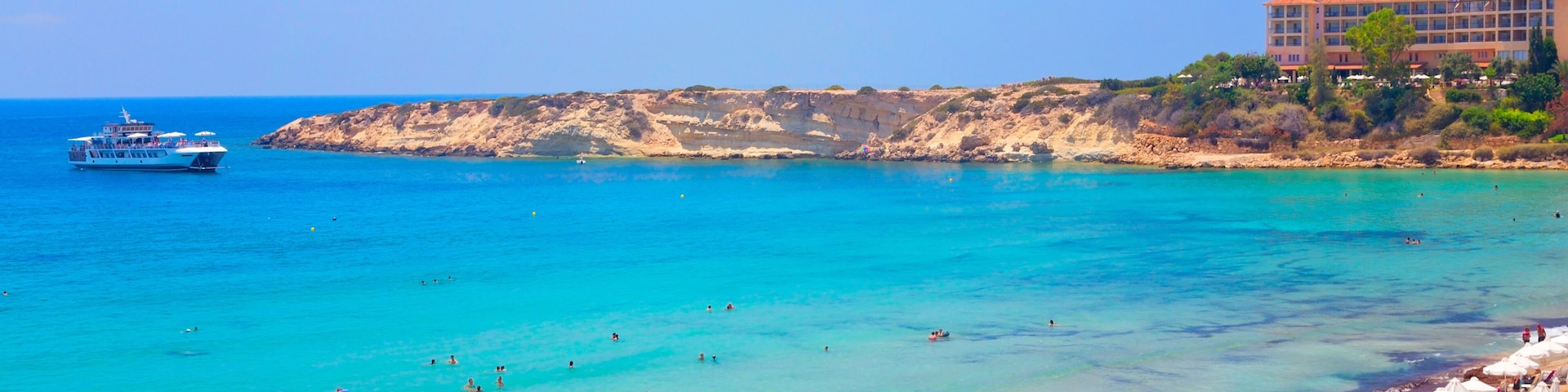 Uma praia com águas turquesa cristalinas, um cruzeiro e um edifício com telhados vermelhos.