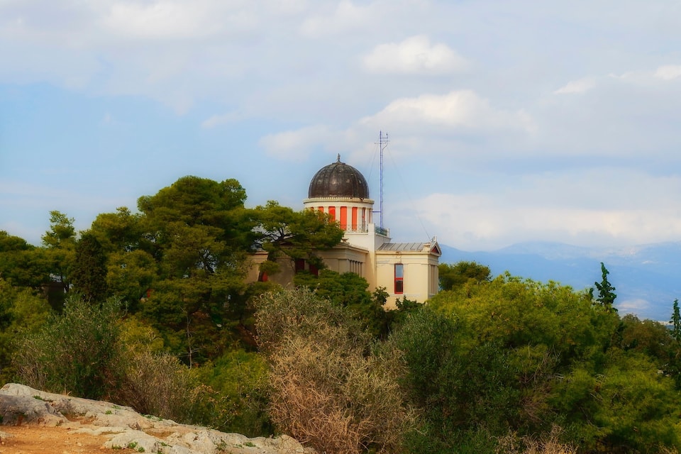 Uma igreja com cúpula e listras vermelhas e brancas, cercada por árvores e pedras.