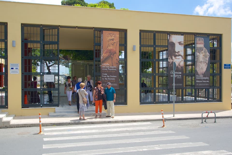 Entrada de um museu com grandes janelas de vidro e cartazes informativos.