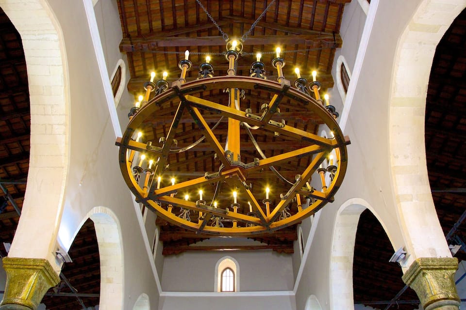 Um lustre grande e ornamentado com múltiplas velas em um edifício histórico com colunas brancas e teto de madeira.