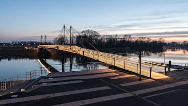 Uma ponte para pedestres sobre um rio calmo ao entardecer.