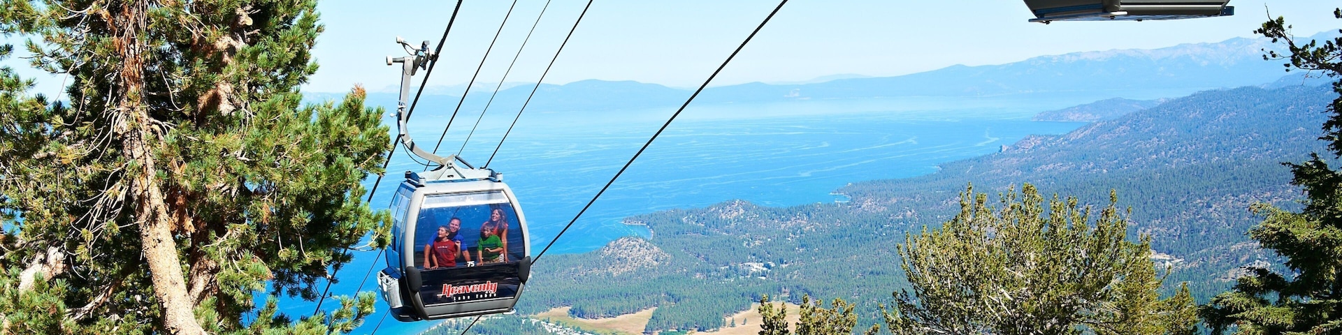 Teleférico com passageiros, paisagem montanhosa e um corpo de água ao longe.