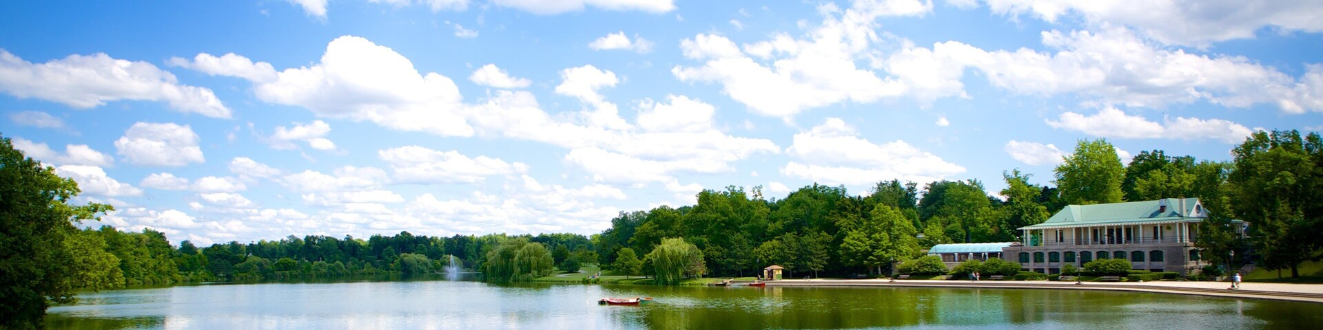 Um lago tranquilo com um edifício grande à direita e vegetação exuberante ao redor.