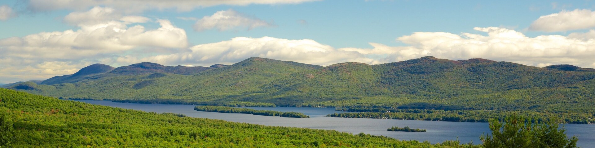 Um lago rodeado por colinas e montanhas verdejantes sob um céu parcialmente nublado.
