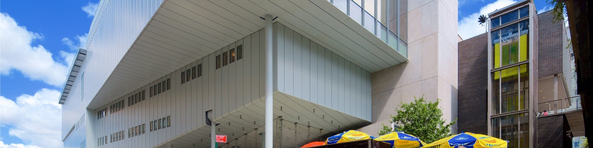 Um edifício moderno com uma grande cobertura e barracas de comida com guarda-sóis.