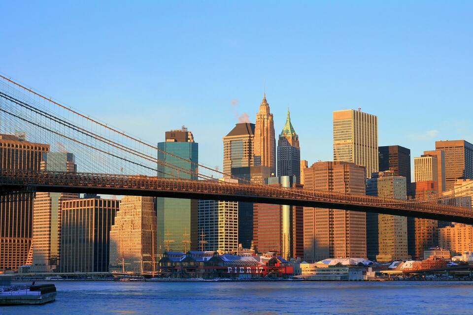 A Ponte do Brooklyn atravessa o rio East, com a paisagem urbana de Manhattan ao fundo.