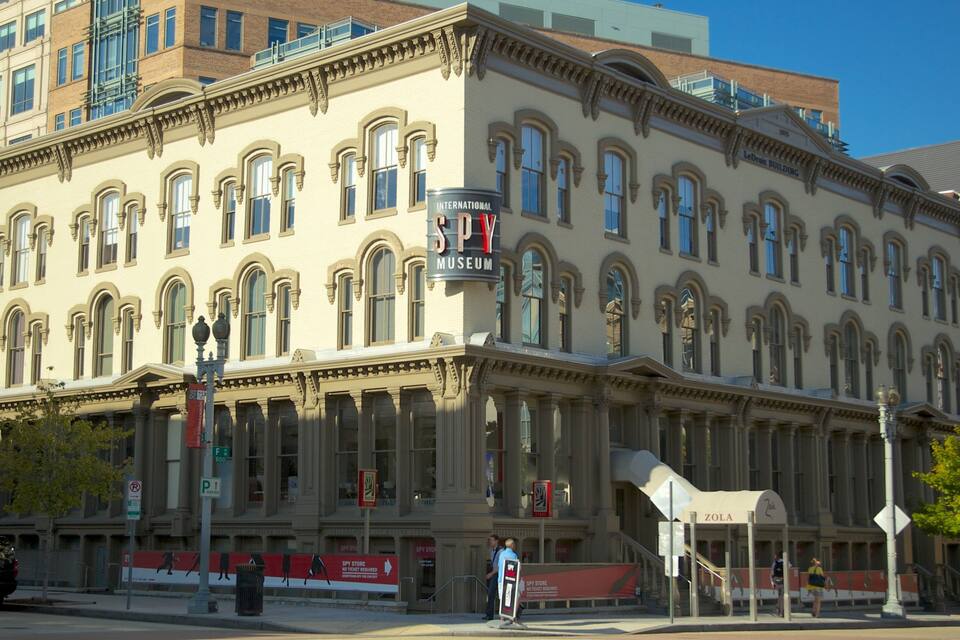 Um edifício histórico com arquitetura elaborada, uma placa para o Museu do Espião e a entrada do restaurante Zola.