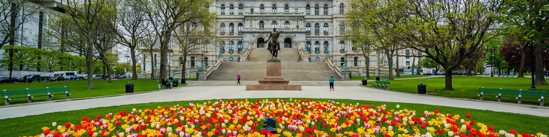 Um edifício grande com telhado vermelho e várias bandeiras, rodeado por um jardim vibrante de tulipas.