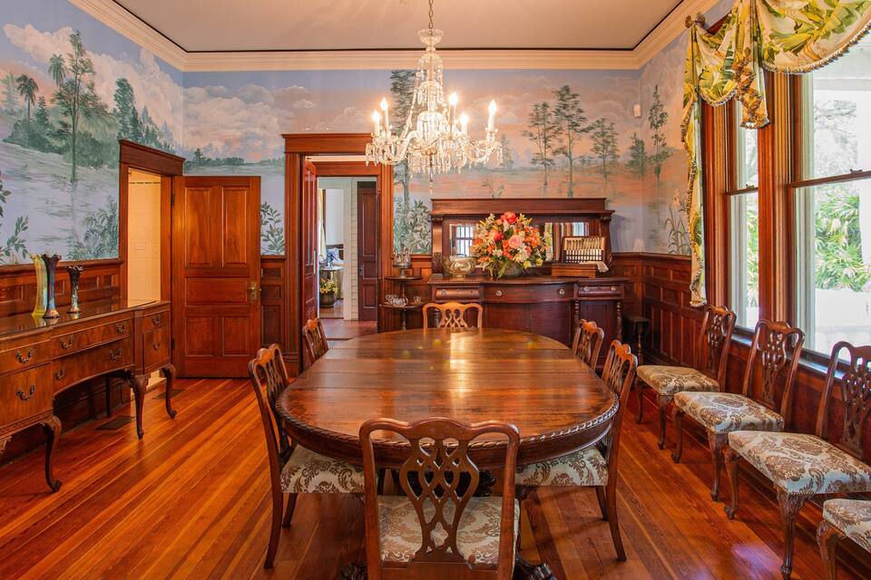 Uma sala de jantar com uma grande mesa de madeira, cadeiras elaboradas e um lustre.