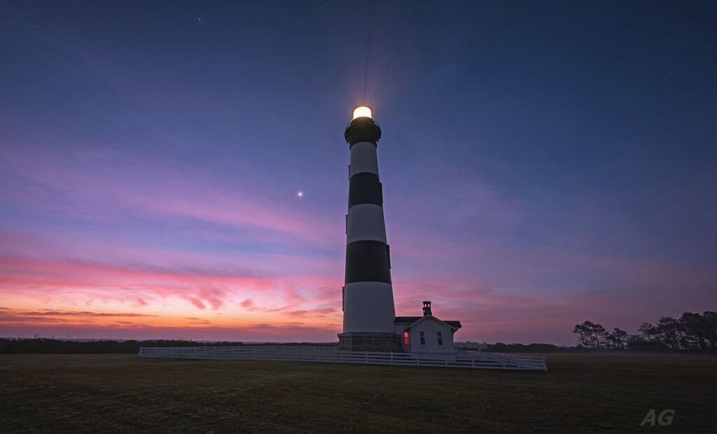 This was one of those on the spur of the moment trips that really leave a few memories behind. This trip transpired during last December, when it was unseasonably warm and Comet Catalina was supposed to be visible in the night sky. I had just been on a long trip to the same location the weekend before and hadn't had much luck with the conditions. So I was in two minds about making the long trip again but I eventually took the call and drove straight off to the coast after work. I arrived too late to catch the sunset that evening but I did manage to catch a sight of Comet Catalina, the Orion Nebula, Andromeda and many other night sky fixtures.

Since it was a last minute trip, I hadn't really made any concrete plans. So rather than drive to a hotel and stay and return in a few hours again for sunrise, I just decided to spend the time at Bodie Island Lighthouse itself. The hood of my car, coupled with a sleeping bag, made for a rather uncomfortable but nonetheless cozy perch to enjoy many hours of star gazing. This wasn't the peak of the Geminid shower but I still caught saw a few bright meteors. Being close to a lighthouse isn't ideal for meteor watching and I wasn't really planning on meteor watching but it was definitely an added bonus.

After several hours of fitful dozing, it was getting close to dawn. I stumbled around groggily, trying to shake the sleep from my mind. It was still pitch dark and although the lighthouse helped with it's friendly light, I couldn't quite see what the sky conditions were like. Nevertheless I setup my camera, composed the shot and just crossed my fingers and hoped for the best. When the light from the sun finally started appearing at the horizon, the entire scene had an almost ethereal quality. The fading light from the lighthouse, Venus and Mars (and Jupiter out of frame) slowly drifting away from sight, the faint traces of the morning mist and the gorgeous sunrise colors at the horizon all contributed to making this a perfect sight.

Thank you for your views and comments.

#colorful #goldenhour #NC #USA #weekend #Lighthouse #roadtrip #Bodie #OBX #blue #bestof5 #history