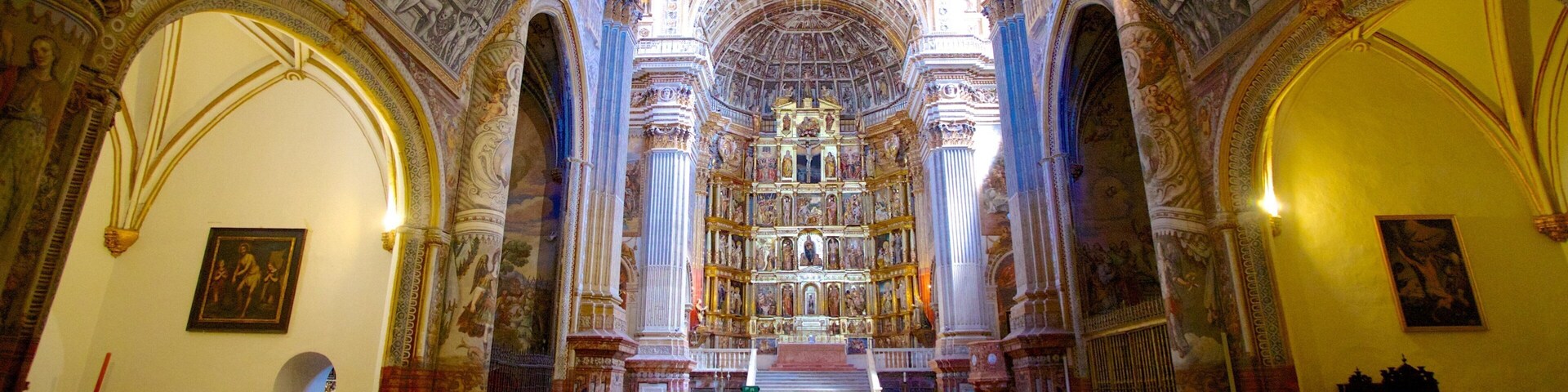Interior de igreja ornamentado, com altos tetos, afrescos detalhados e fileiras de bancos.