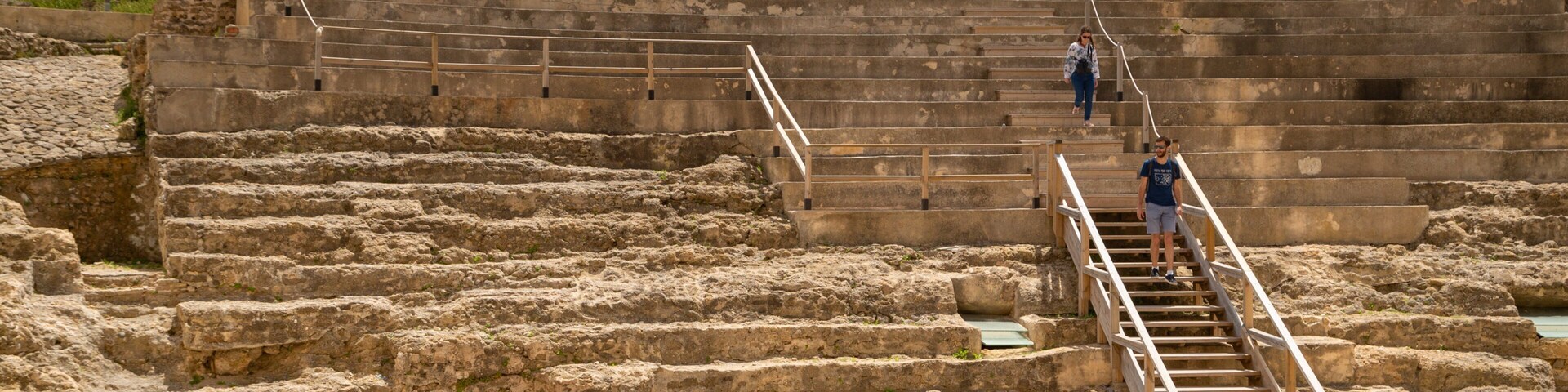 Degraus de pedra antiga que levam a um muro, com palmeiras ao fundo.