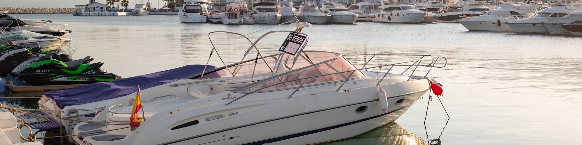 Uma marina com vários barcos atracados, uma paisagem urbana ao fundo e céu claro.