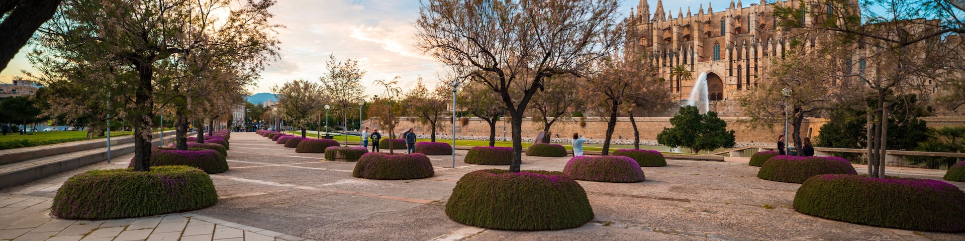 Um jardim bem cuidado com sebes aparadas e um edifício histórico ao fundo.