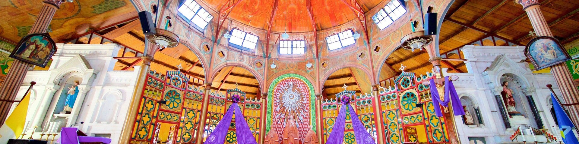 Interior de igreja com teto vibrante e ricamente decorado, vitrais e altar central.