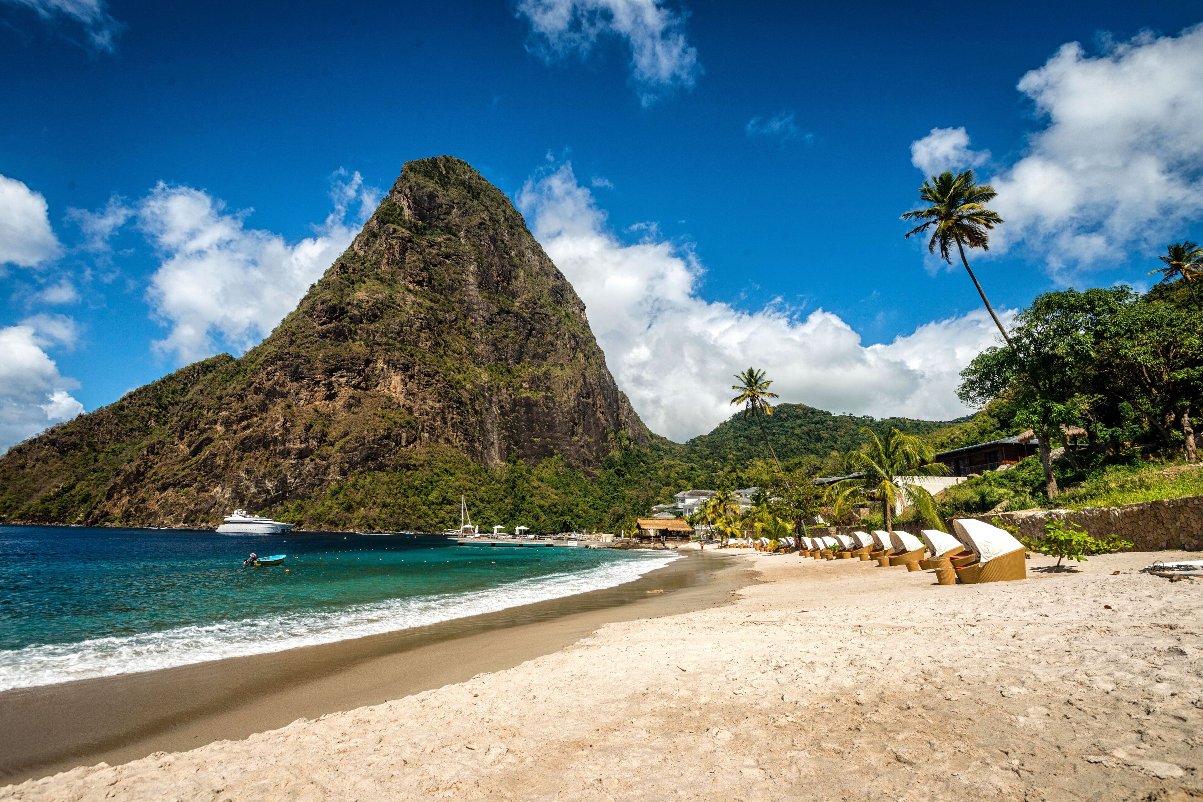 Uma praia com uma montanha imponente, água azul cristalina e uma fileira de espreguiçadeiras.