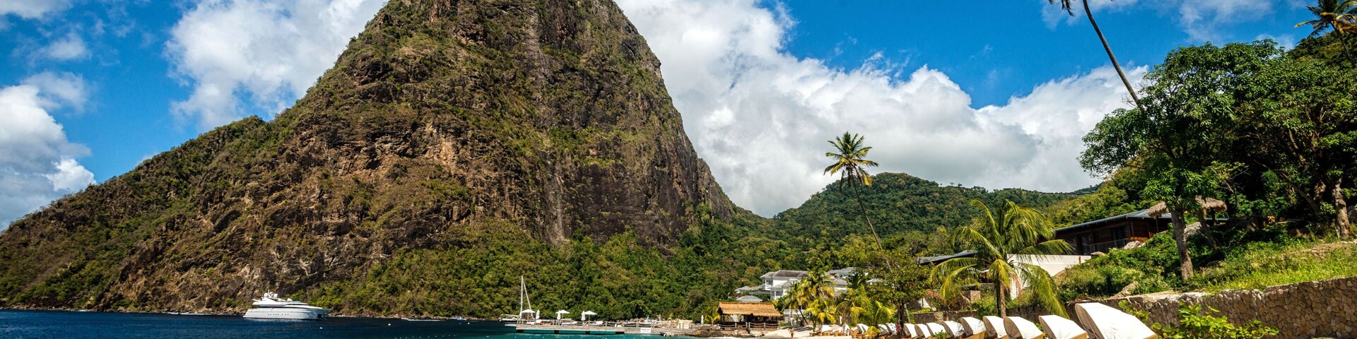 Uma praia com uma montanha imponente, água azul cristalina e uma fileira de espreguiçadeiras.