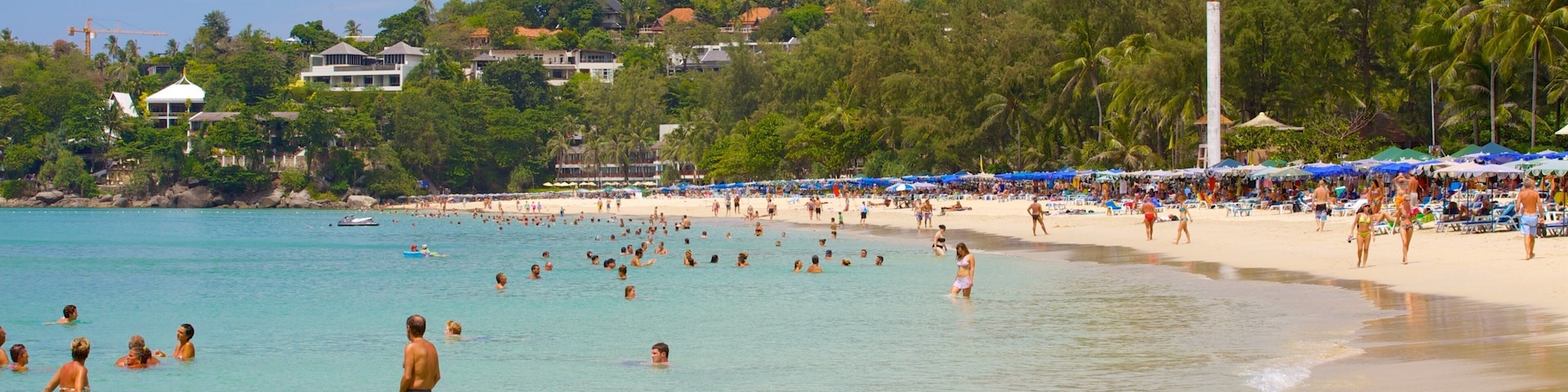 Uma praia movimentada com águas turquesa cristalinas, palmeiras e guarda-sóis.