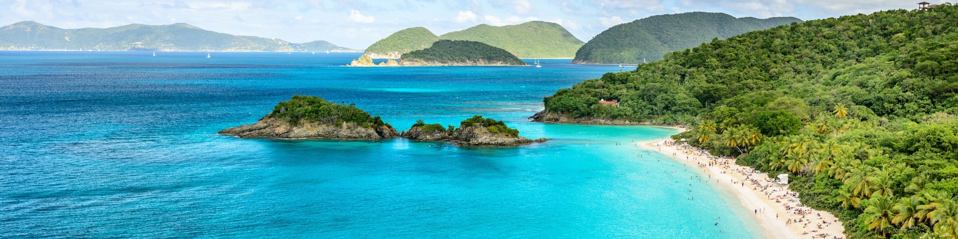 Um mar azul-turquesa, uma praia e colinas verdejantes.