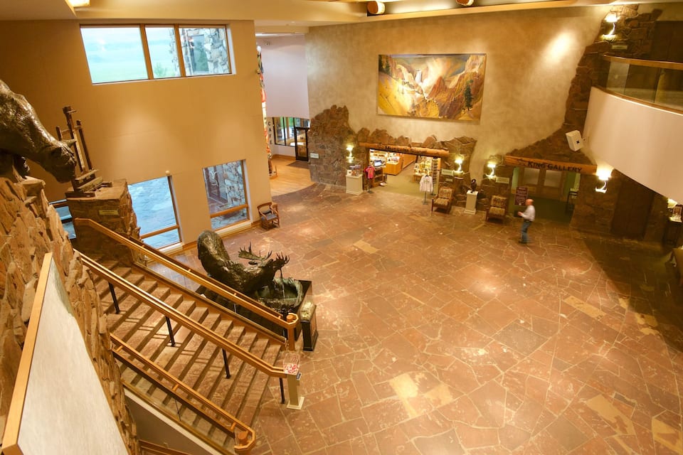 Interior de museu com paredes de pedra, uma pintura grande e uma escadaria.
