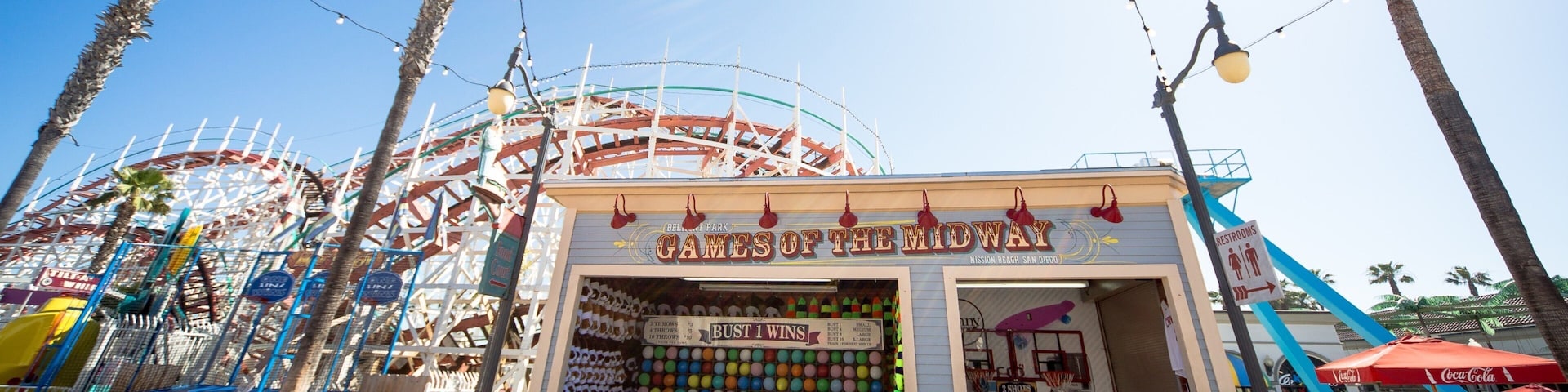 Barraquinha de jogo de carnaval com um letreiro escrito 'Games of the Midway' e uma roda-gigante ao fundo.