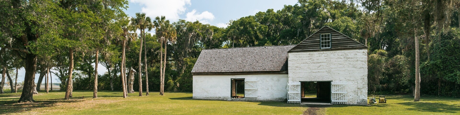 Um edifício branco com telhado escuro, cercado por árvores e um campo gramado.