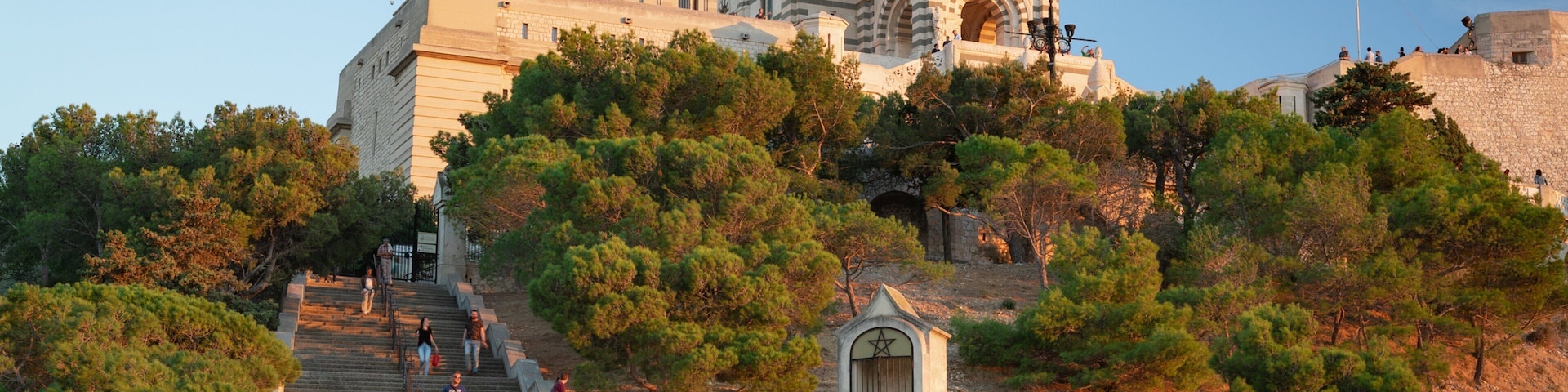 Uma catedral histórica com uma torre de sino imponente, rodeada por vegetação exuberante e uma escadaria de pedra que a leva até ela.
