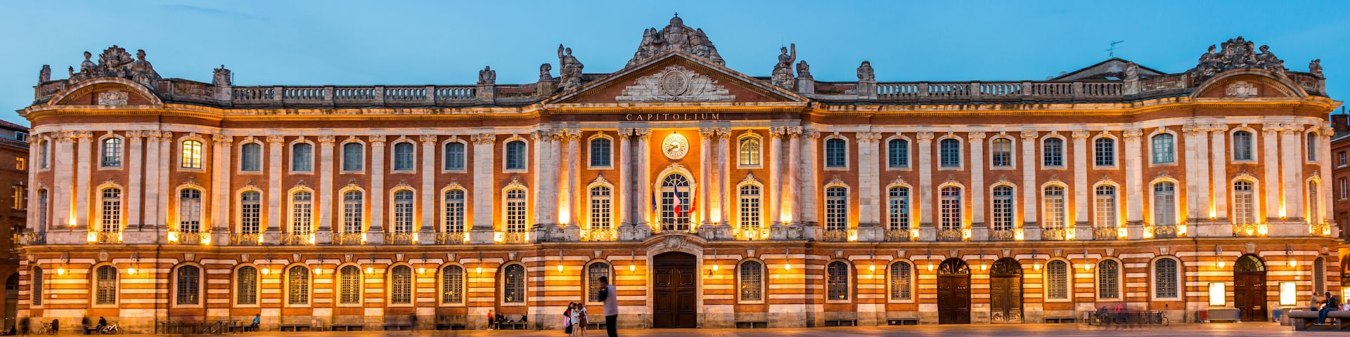 A fachada do Museu do Louvre ao entardecer, destacando arquitetura clássica e a icônica entrada em vidro piramidal.