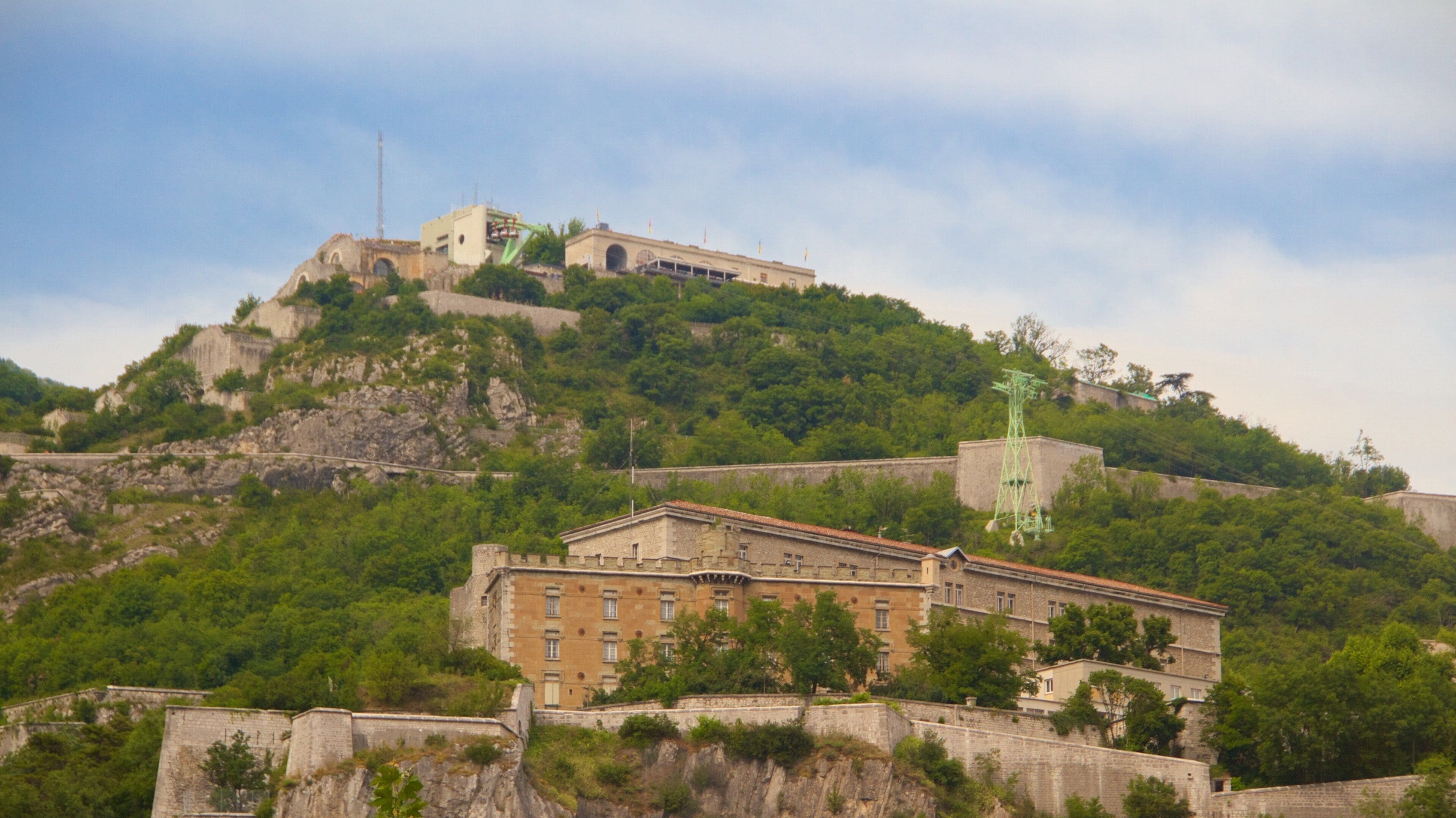 Uma colina histórica com edifícios antigos, uma torre de vigia e vegetação exuberante.