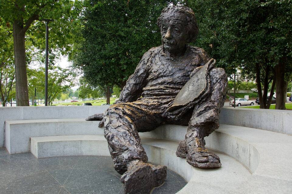 Estátua de bronze de um homem sentado em um parque.